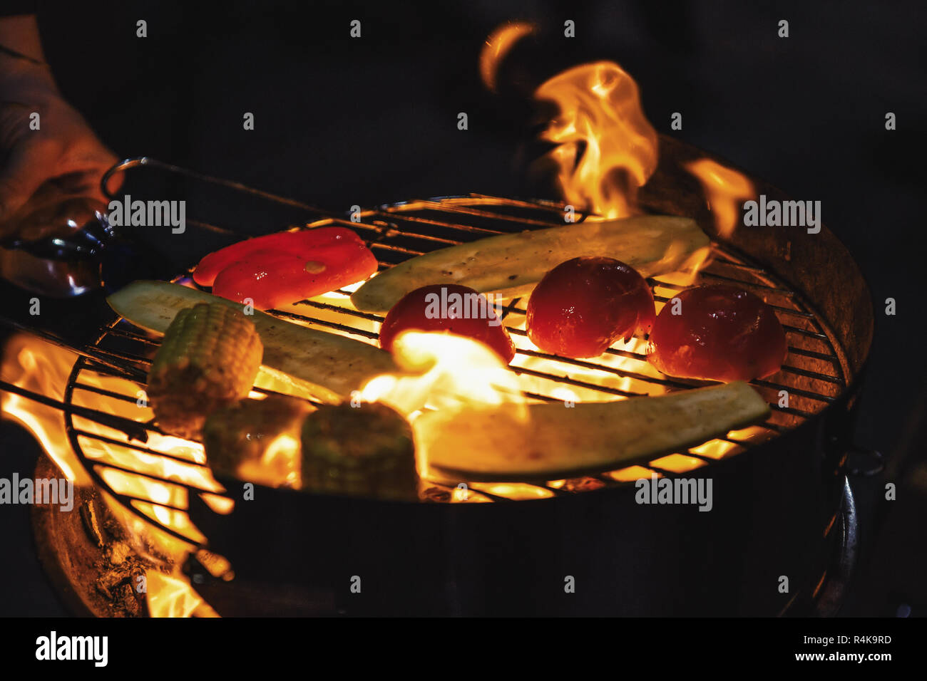 Cooking vegetables on open fire grill. The cook grills tomatos and ...