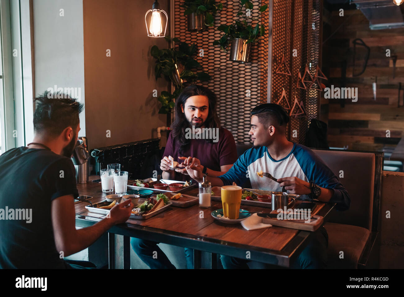 Multiracial friends eat breakfast in cafe. Young arabic men chat while ...