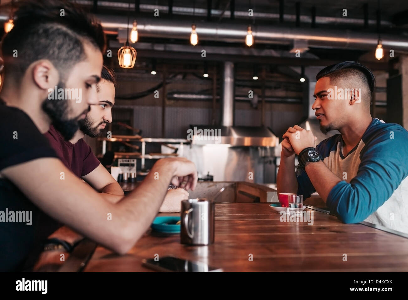 Group of mixed race young men talking and laughing in lounge bar ...
