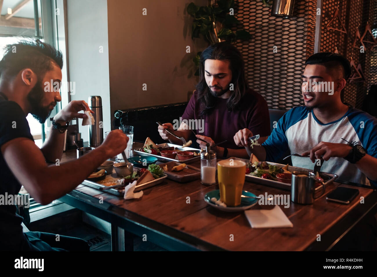 Multiracial friends eat breakfast in cafe. Young arabic men chat while ...