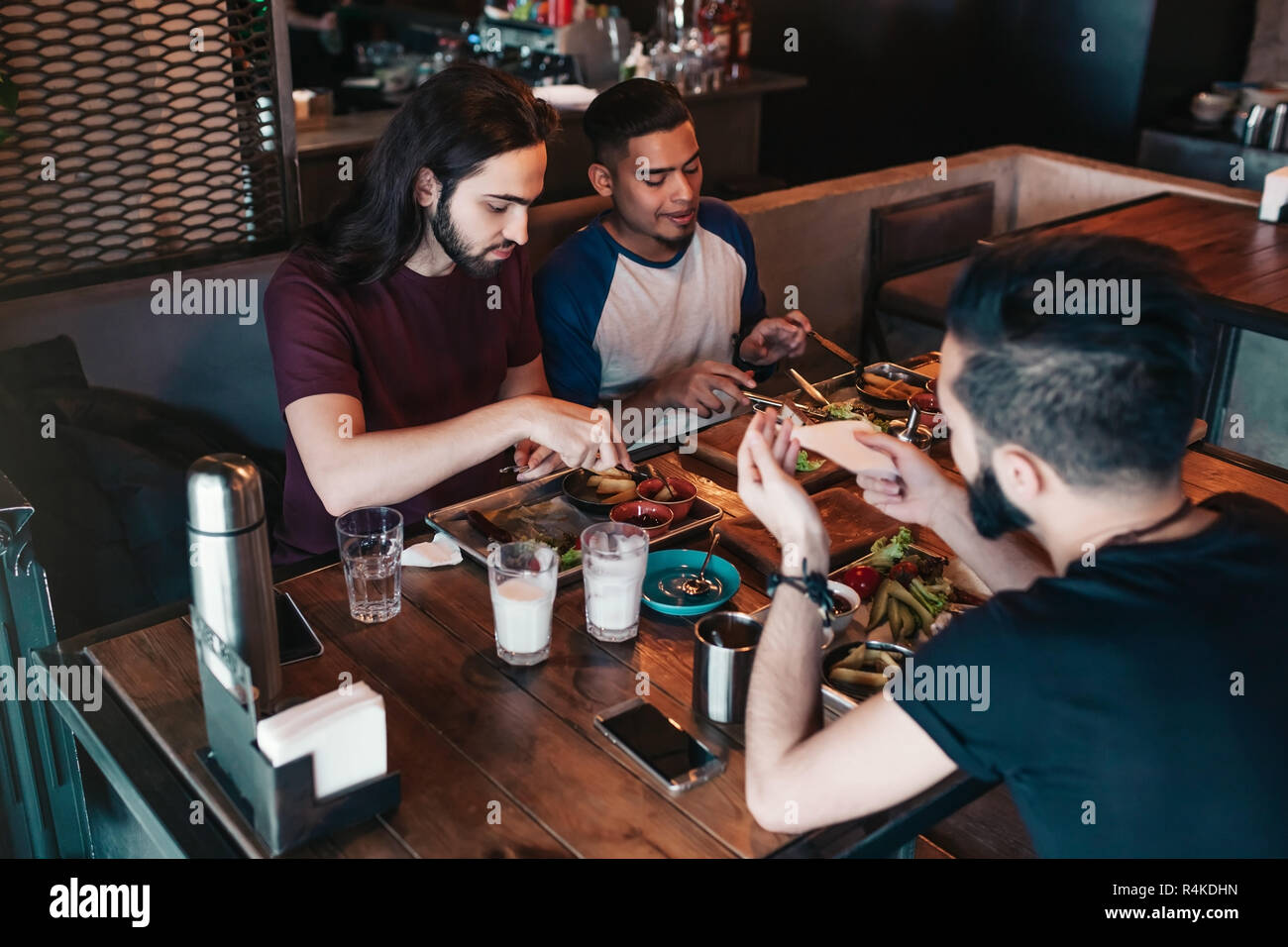 Multiracial friends eat breakfast in cafe. Young arabic men chat while ...