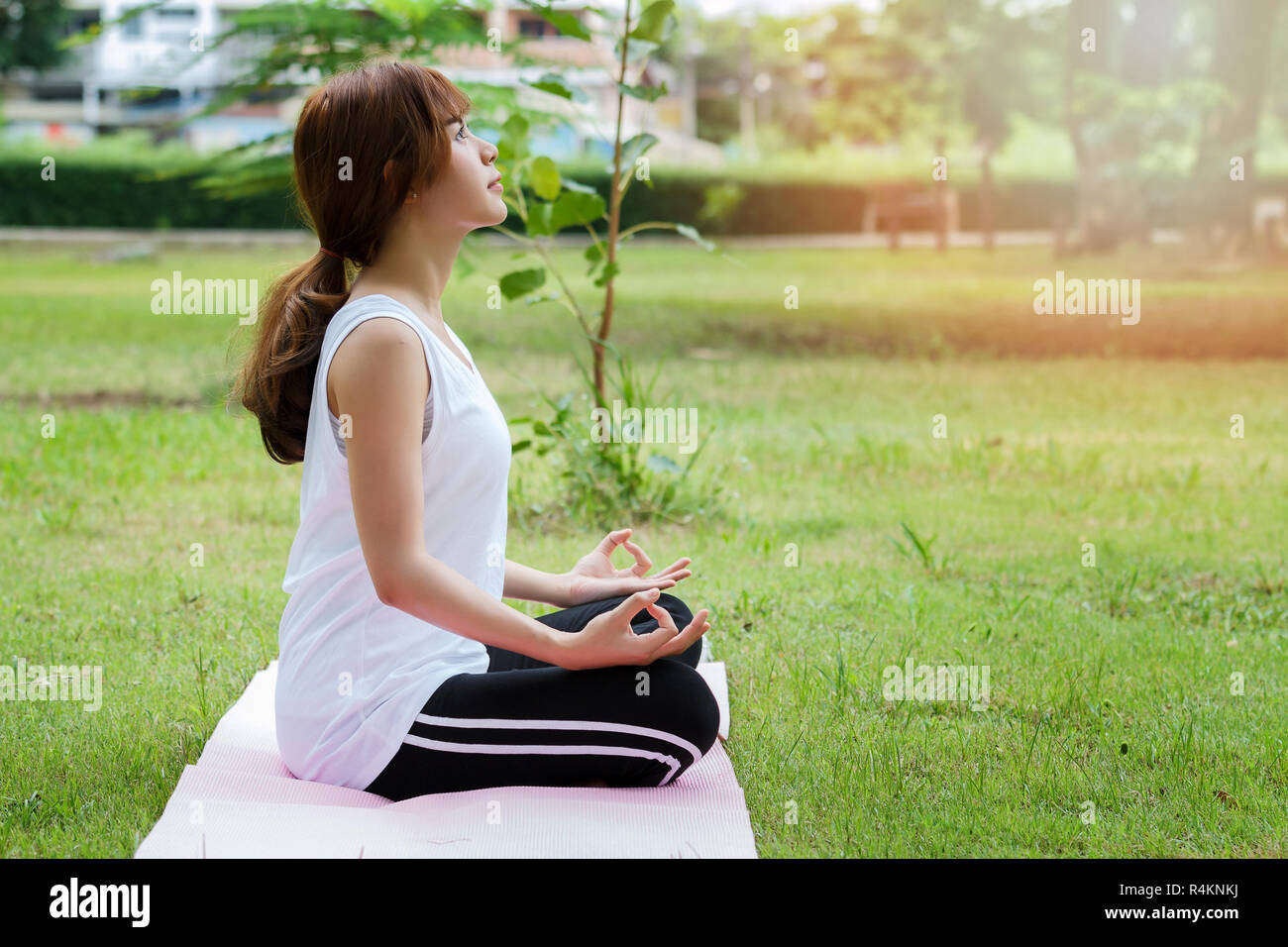 Young asian woman in sportswear meditating while sitting in lotus pose ...