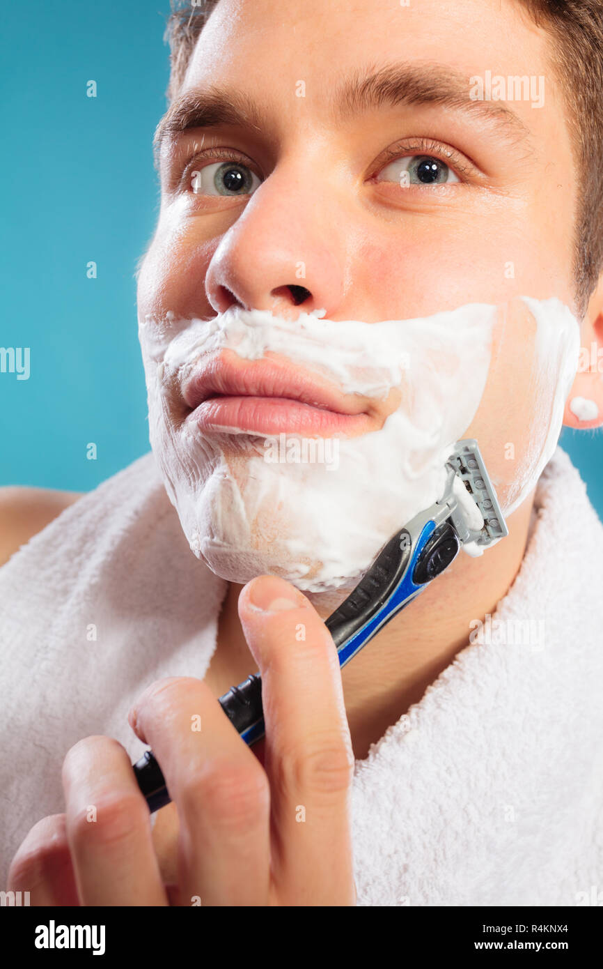 Young man shaving using razor with cream foam. Handsome guy removing face beard hair. Skin care ...