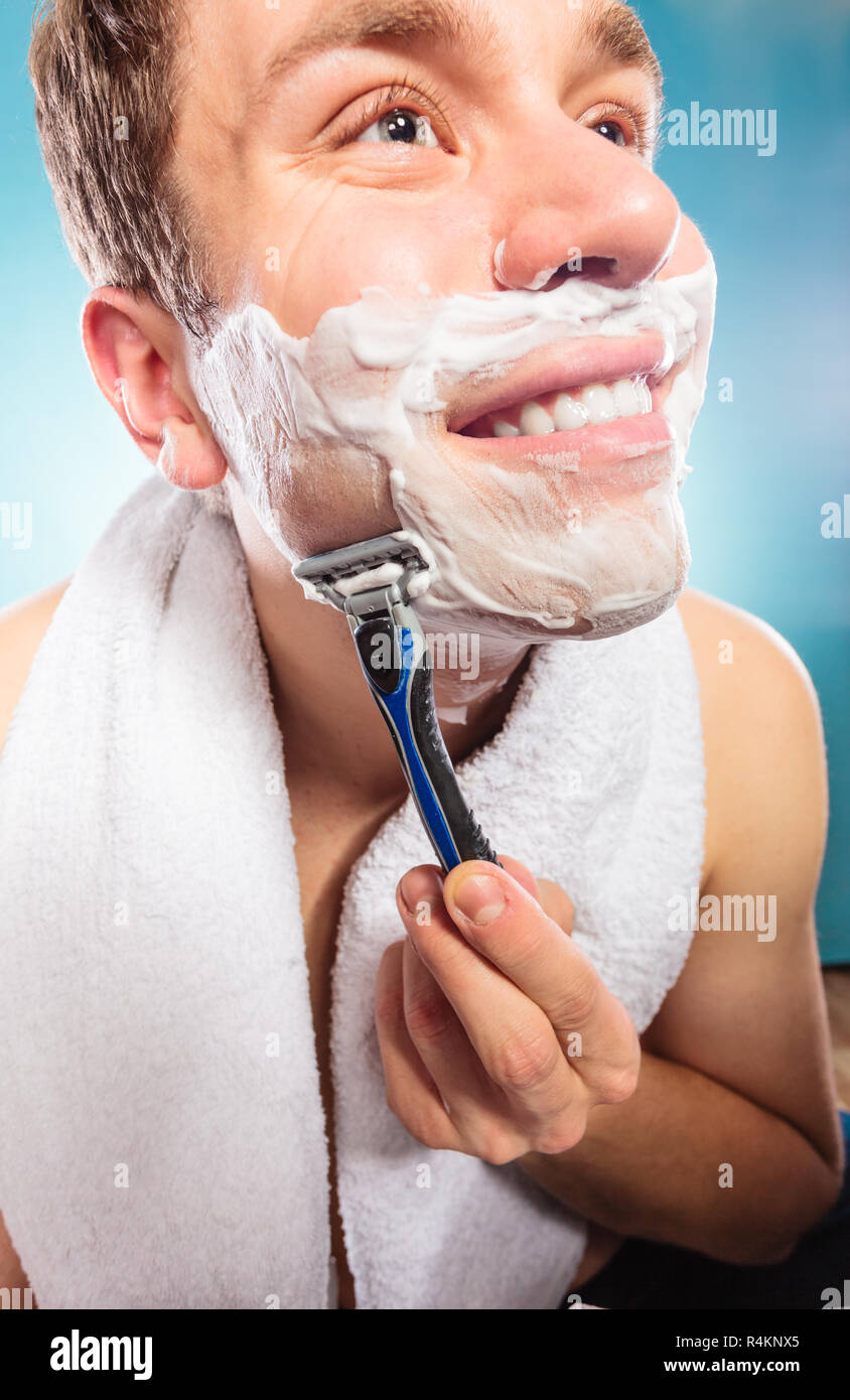 Happy smiling man shaving using razor with cream foam. Handsome guy removing face beard hair ...