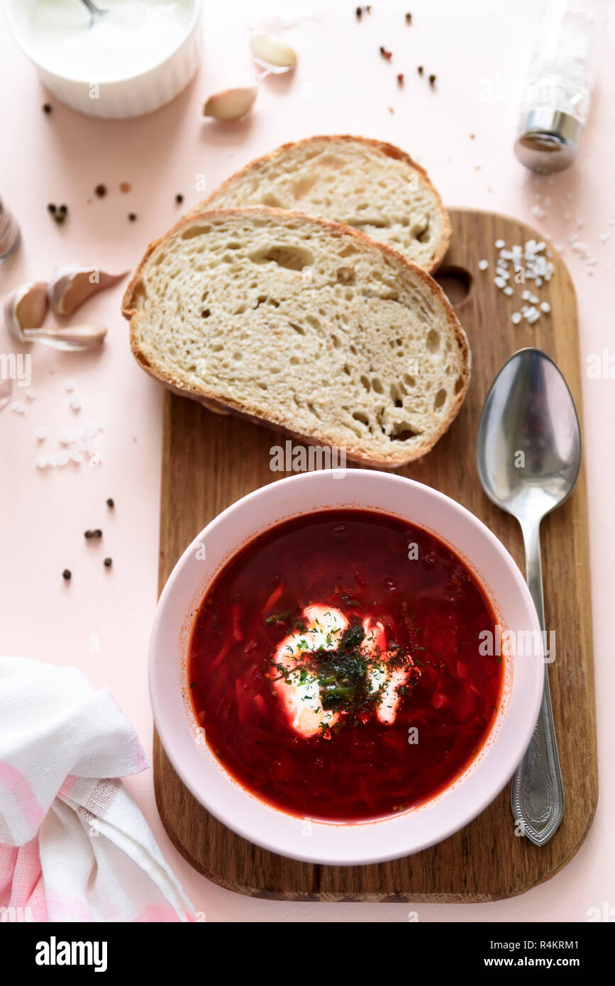 Red borscht soup in pink bowl with sour cream, bread, garlic and spices ...