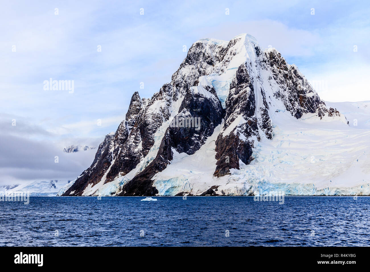 Gigantic steep stone cliff covered with snow and sea in foreground ...