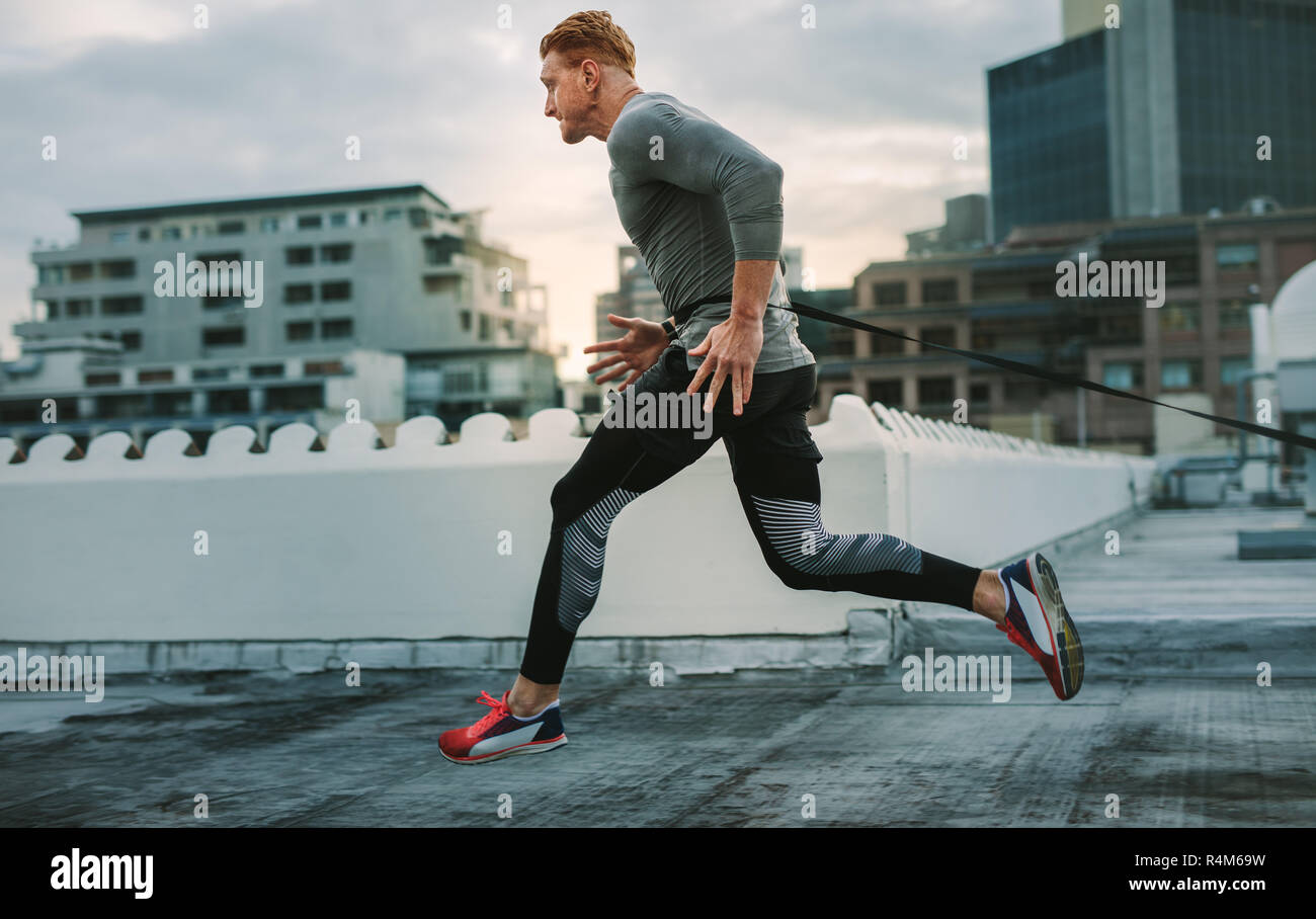 Male athlete doing drag running on rooftop. Side view of a fitness man ...