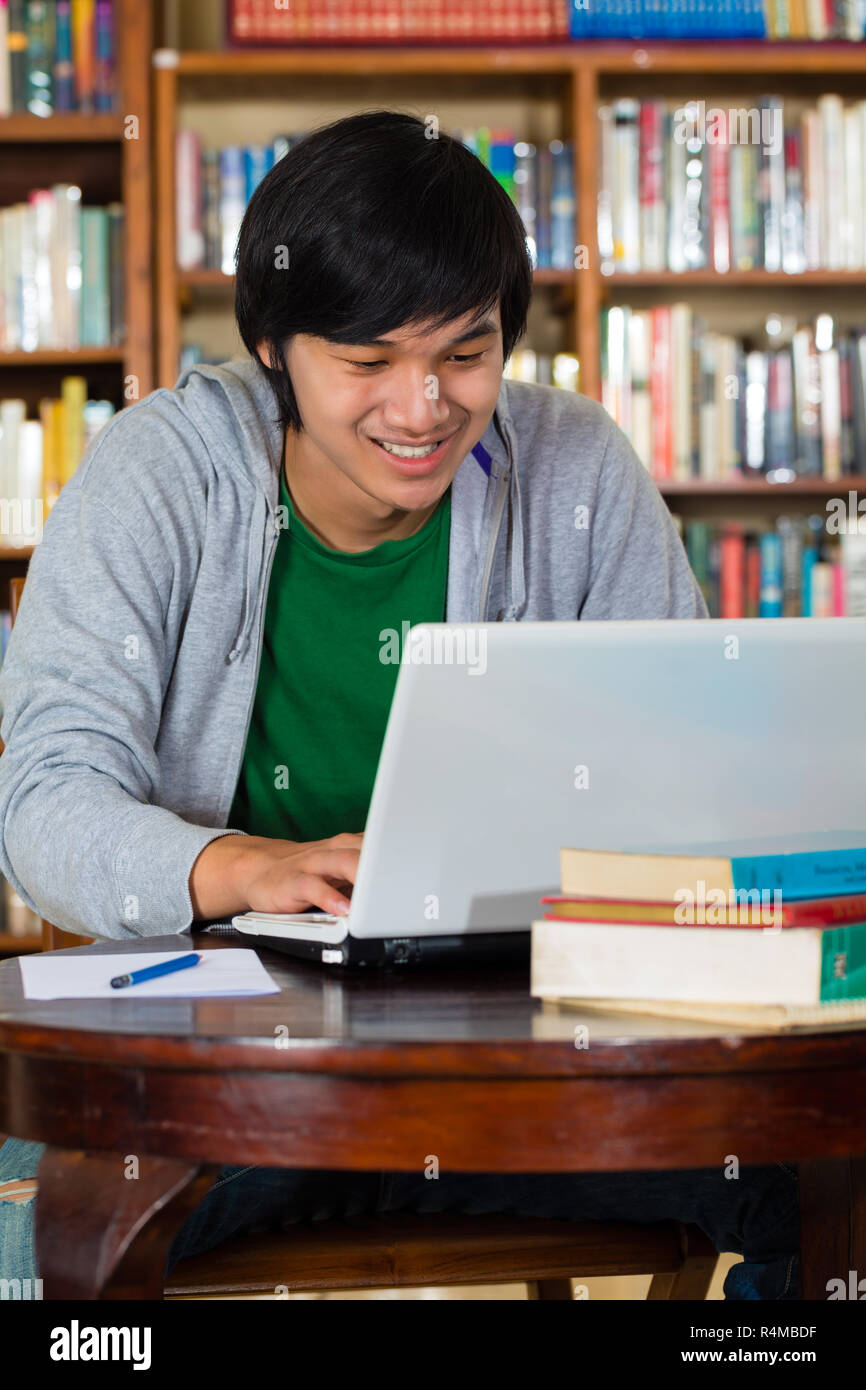 Asian man in library with laptop Stock Photo - Alamy