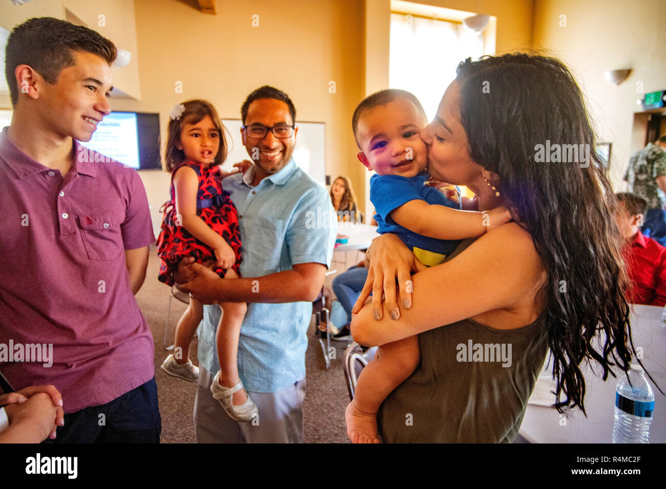 A Hispanic couple hug their young children while waiting for a class on ...