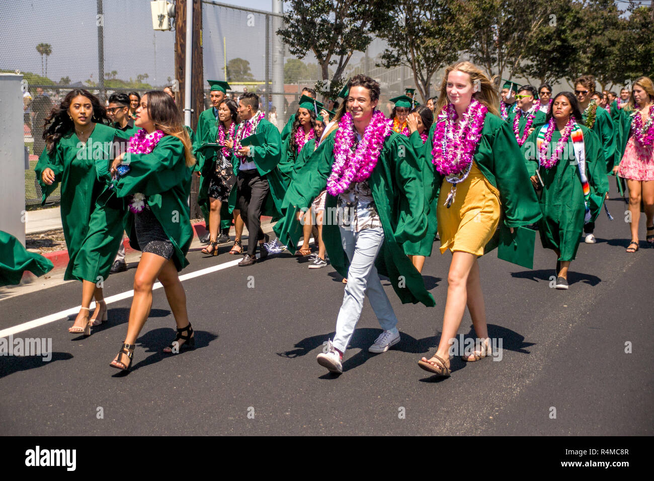 Happy high school graduates, many wearing leis, march to meet audience ...
