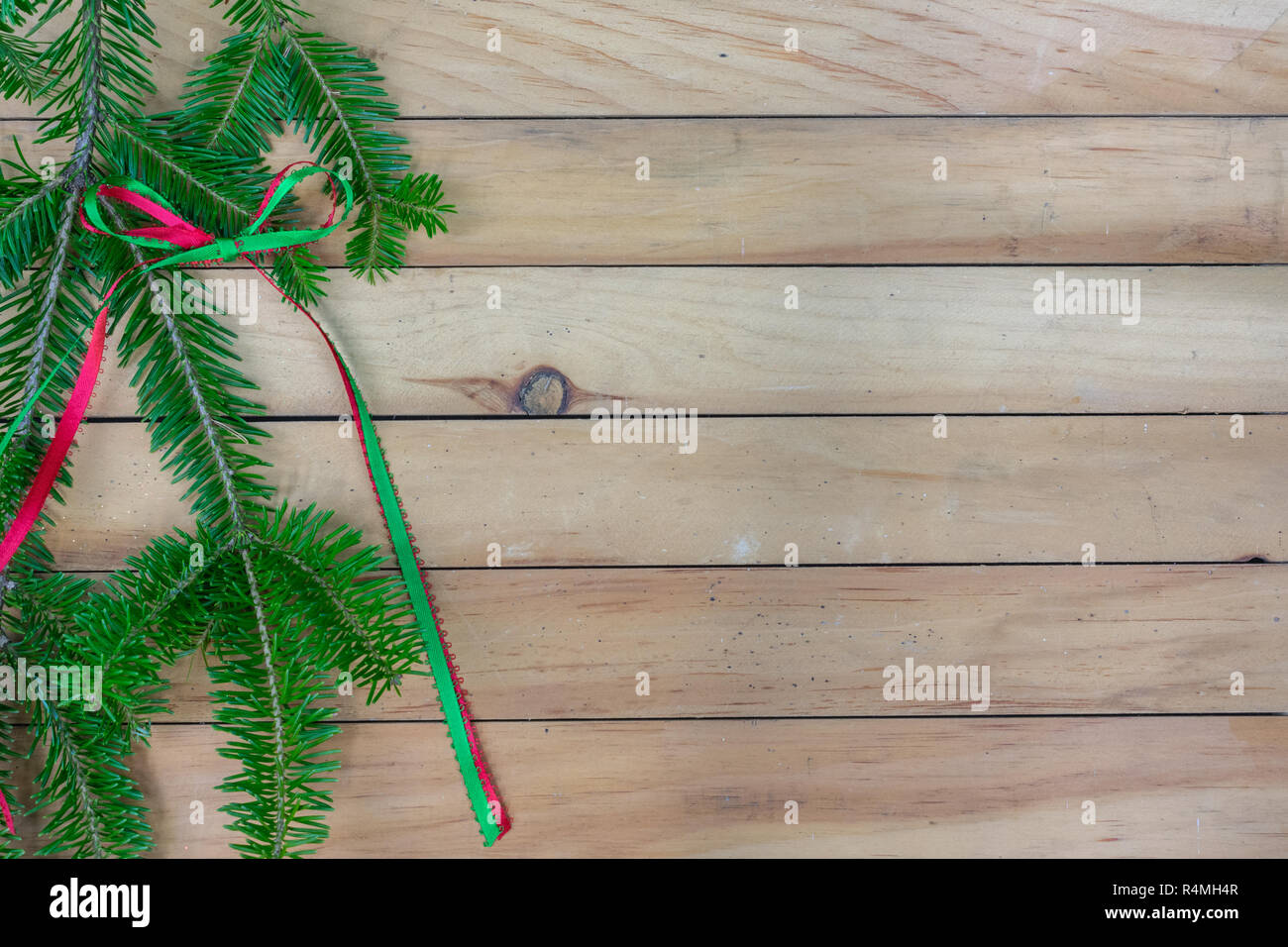 A spruce bough with a red and green bow on a wooden slat background ...