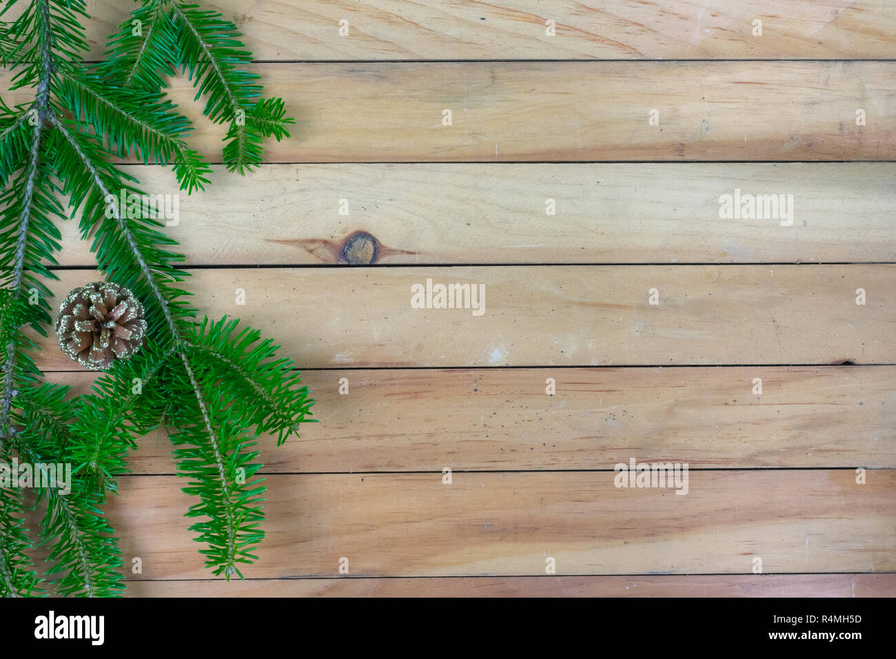 A spruce bough with a glittered pine cone on a wooden slat background ...