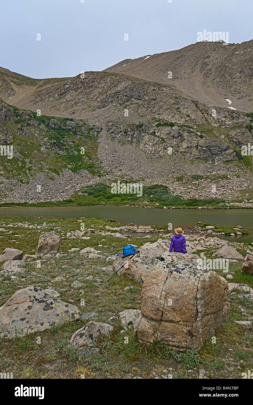 Woman resting on rock by lake while hiking in Herman Gulch, Colorado ...