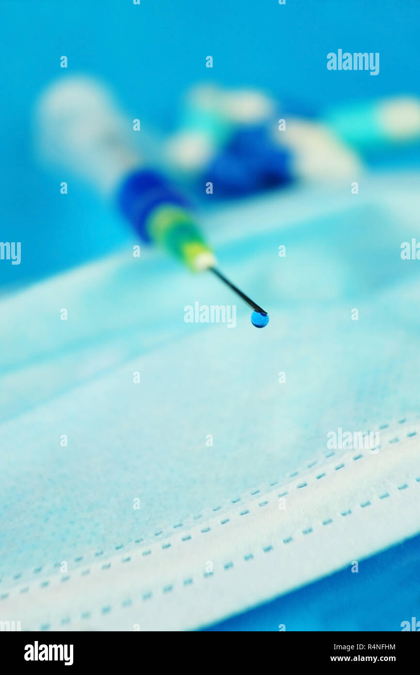 A detailed macro of a syringe by pills with a blue liquid drop through ...