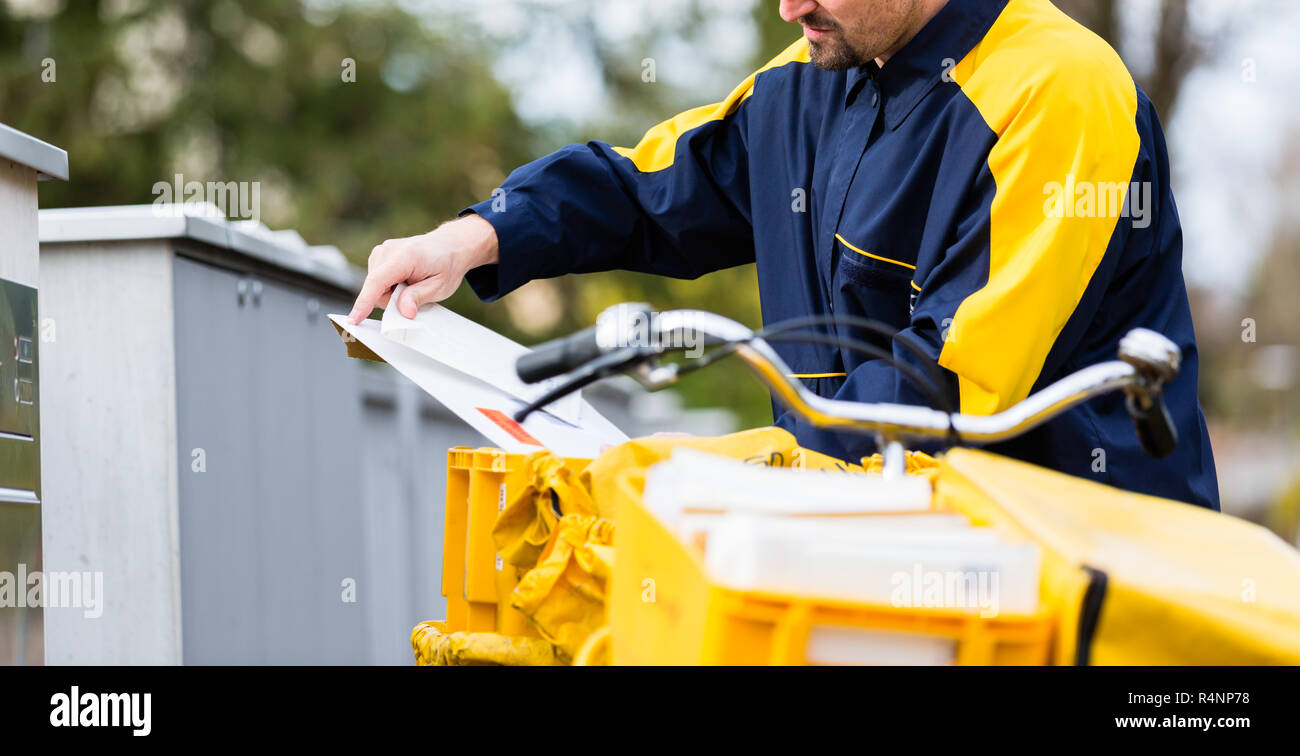 Postman delivering letters to mailbox of recipient Stock Photo - Alamy