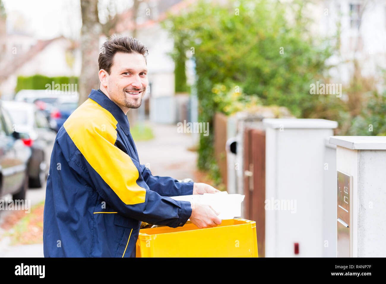 Postman delivering letters to mailbox of recipient Stock Photo - Alamy