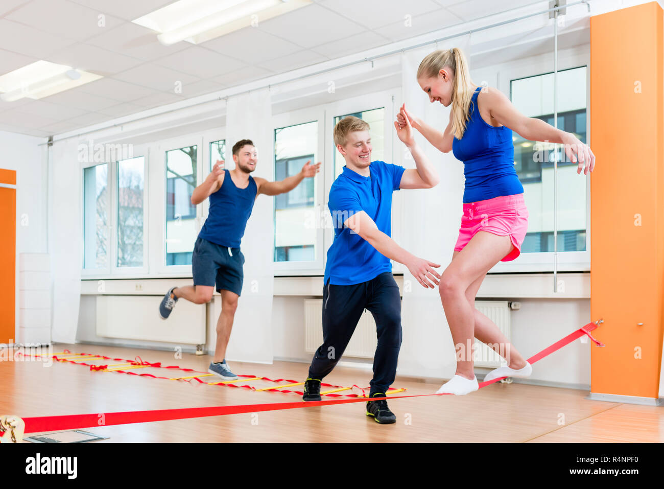 Physio practicing slacklining with athletes in gym Stock Photo - Alamy