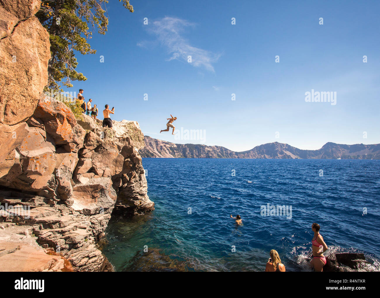 Young people wait on a rock outcrop and swim or jump into the deep blue ...