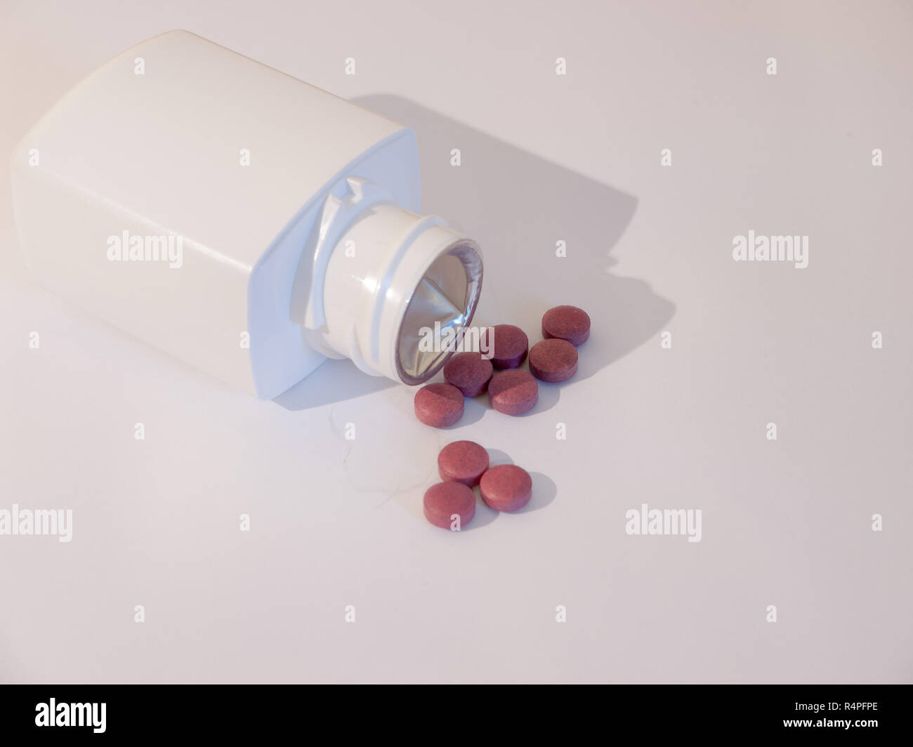 a generic white bottle with red tablet pills poured out of it dispensed ...