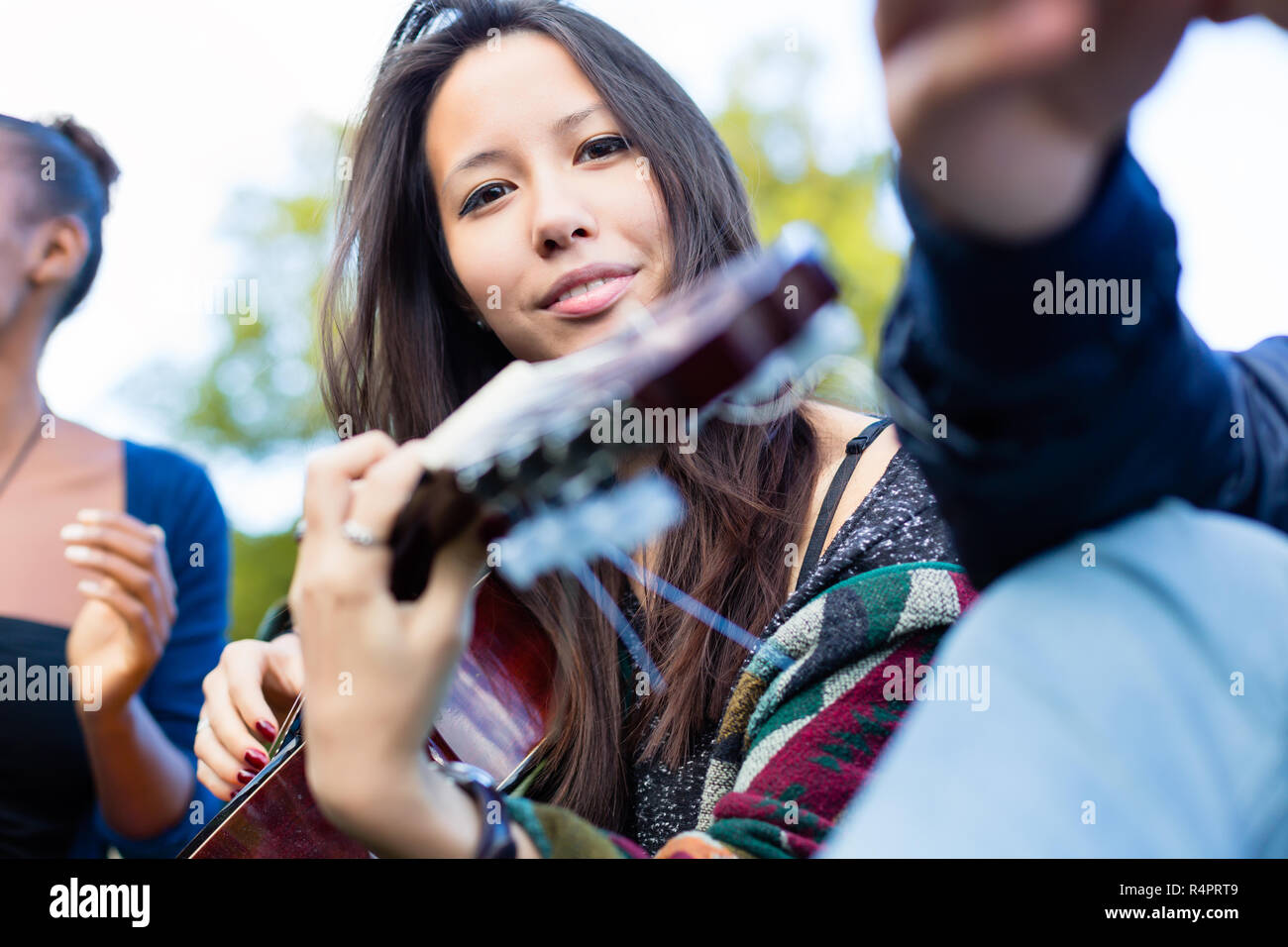 Guitar player girl making music with friends in park Stock Photo - Alamy