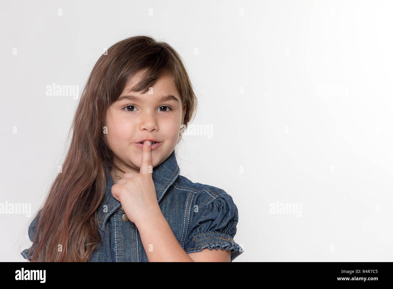 Portrait of slightly smiling little girl gesturing shush Stock Photo ...