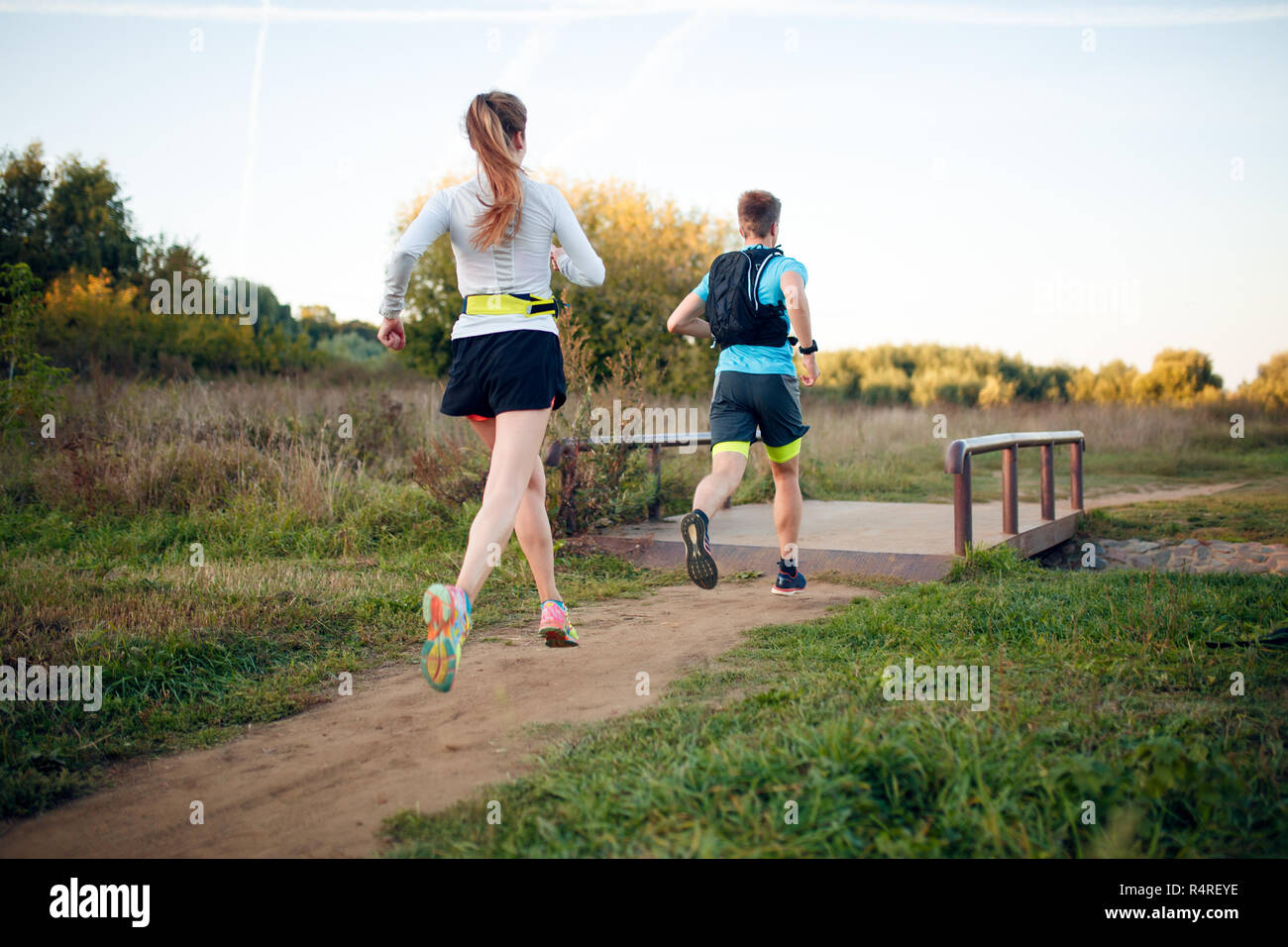 Image on back of sportive woman and man running through park on summer ...