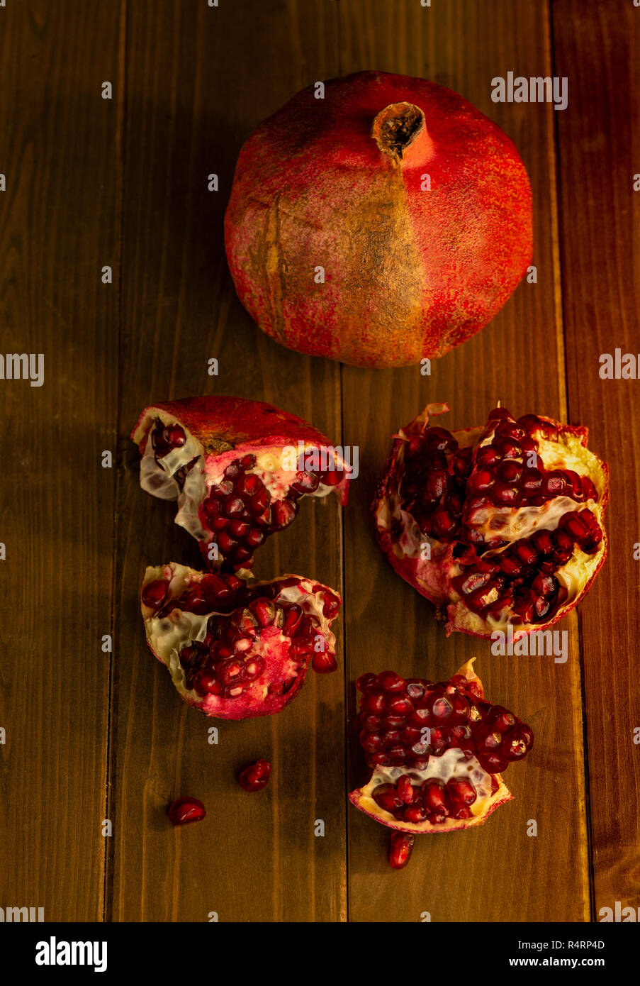 Two pomegranate fruits, one whole and one open, against wooden table ...