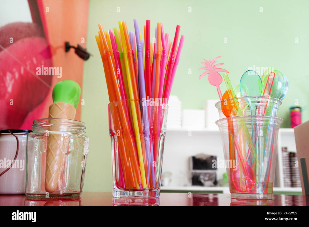 Colorful drinking straws in glass, plastic spoon and plastic spatula ...