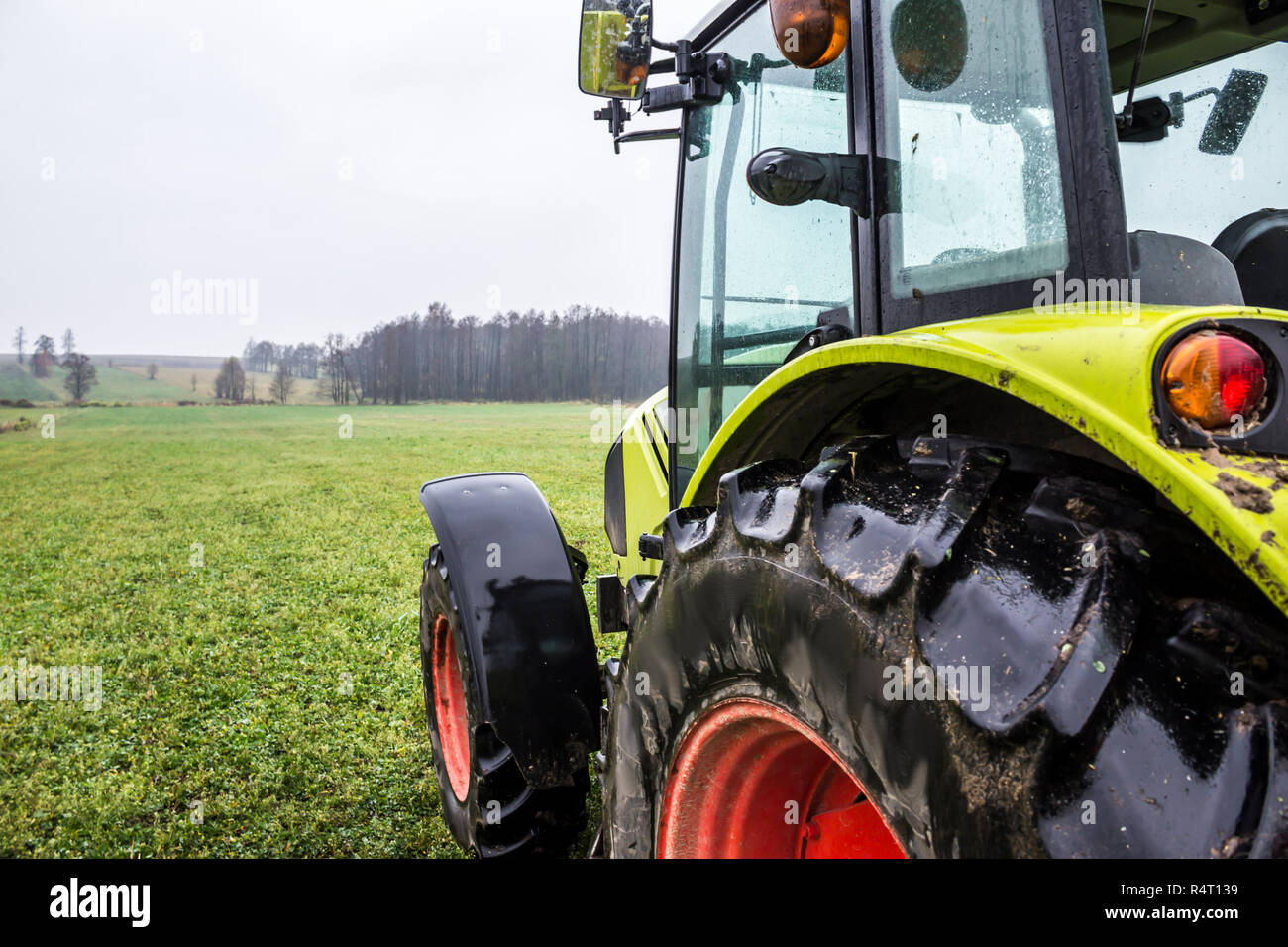 Rainy day in late autumn. Tractor on the edge of a meadow with green ...
