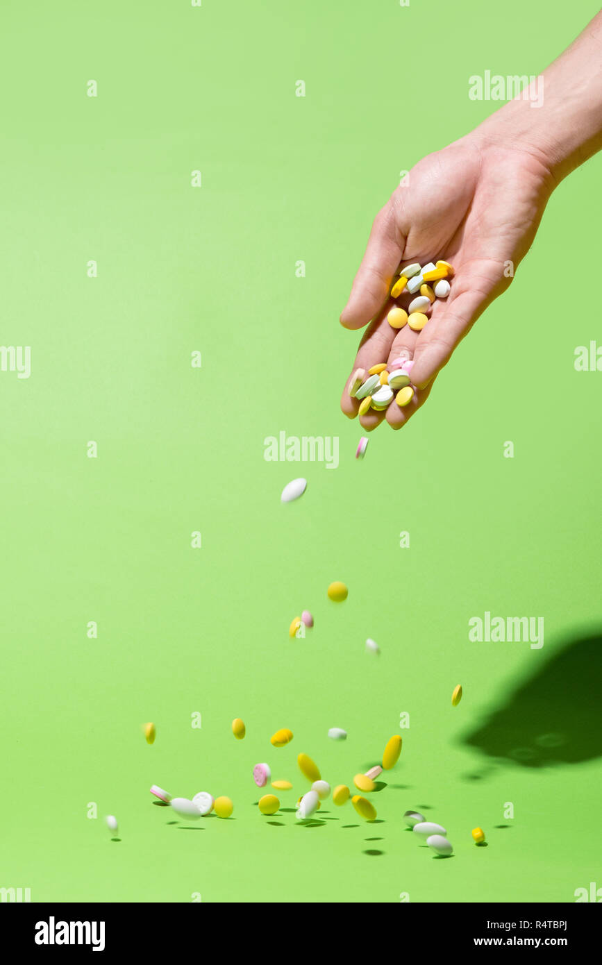 Colored pills falling from hand on green background Stock Photo - Alamy