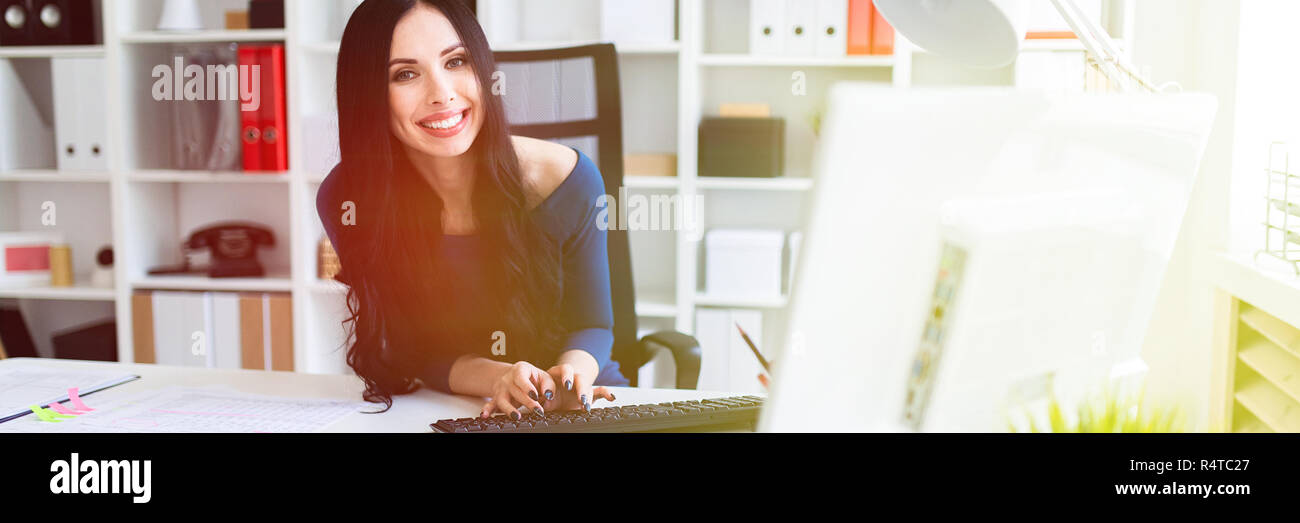 A young girl is sitting at the office at the table and typing text on ...