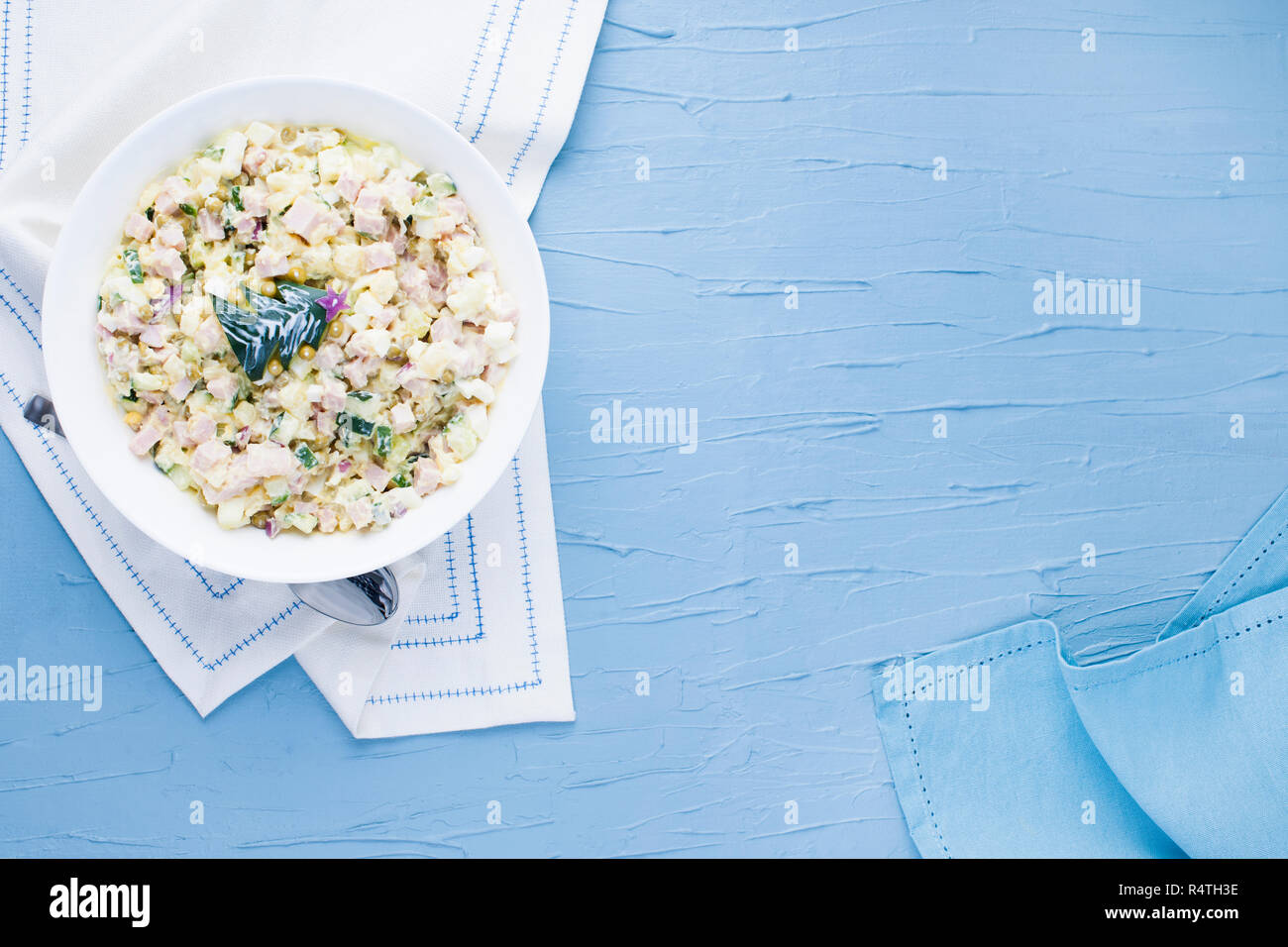 Russian salad in a plate on a blue background. Free space for text. Top ...