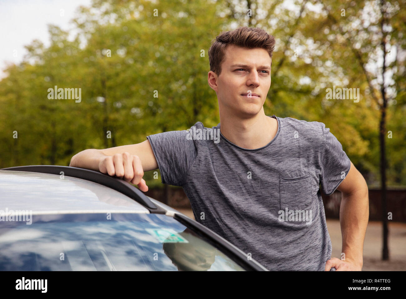 Portrait young man leaning on car, looking away Stock Photo - Alamy