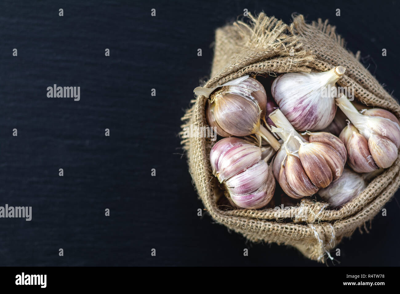 Garlic in a sack of old cloth. Fresh garlic on a black stone surface ...