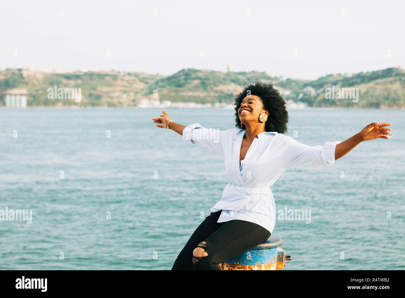 Carefree young woman with arms outstretched at waterfront, Belem ...