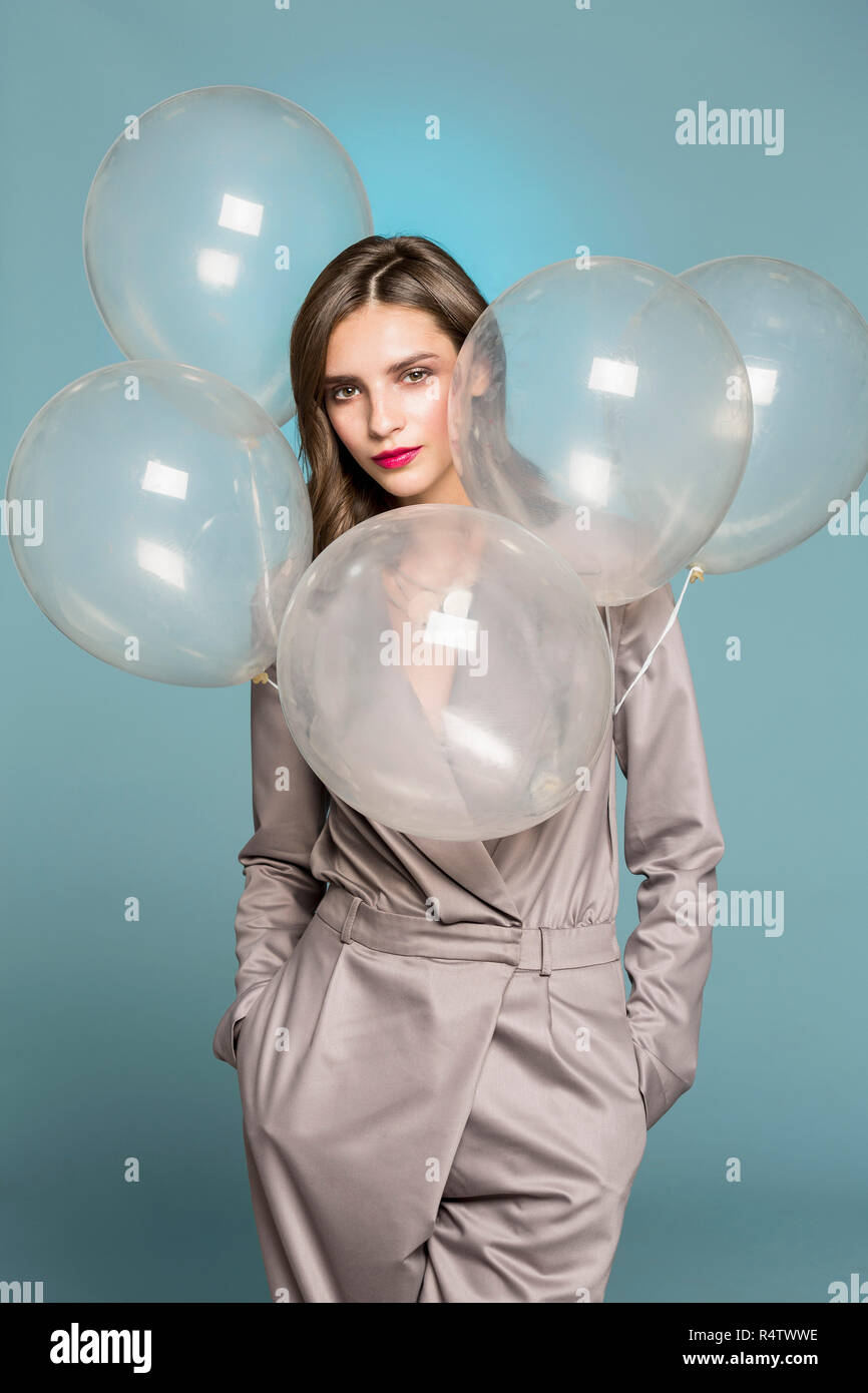 Portrait of female fashion model standing with balloons against blue ...