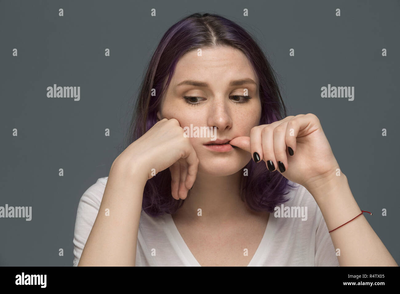 Portrait of a young woman with dyed hair biting thumb and looking down ...