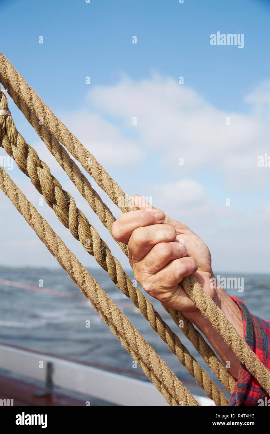 Man holding rope, adjusting rigging on boat Stock Photo - Alamy