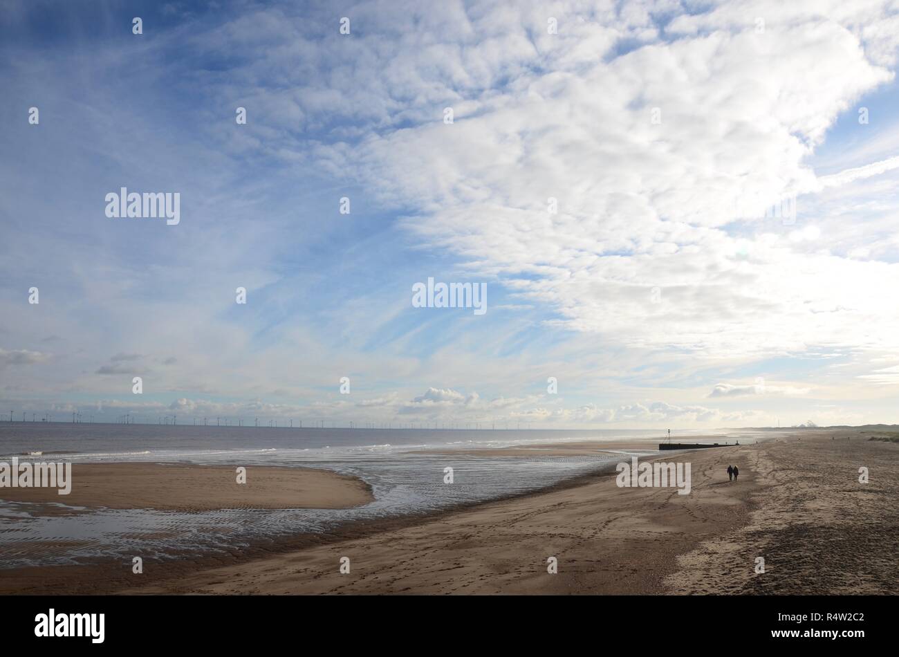Empty seascape with big open sky, clouds, two figures walking and wind ...