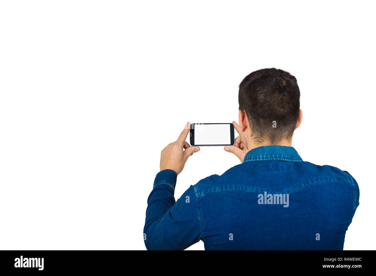 Rear view of young man, blue jeans jacket, holding a smart cell phone ...