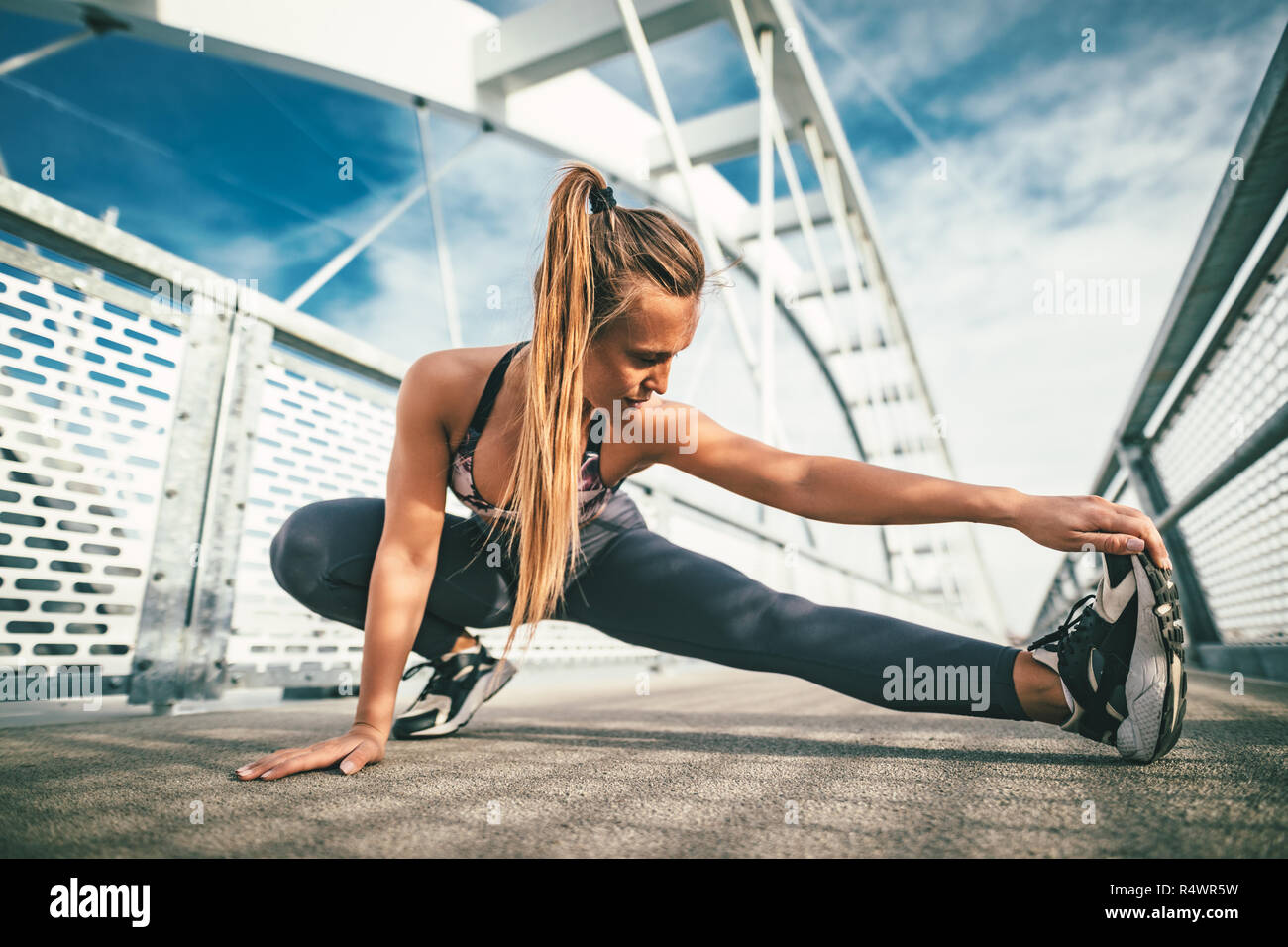 Young female runner doing stretching exercise on a river bridge ...