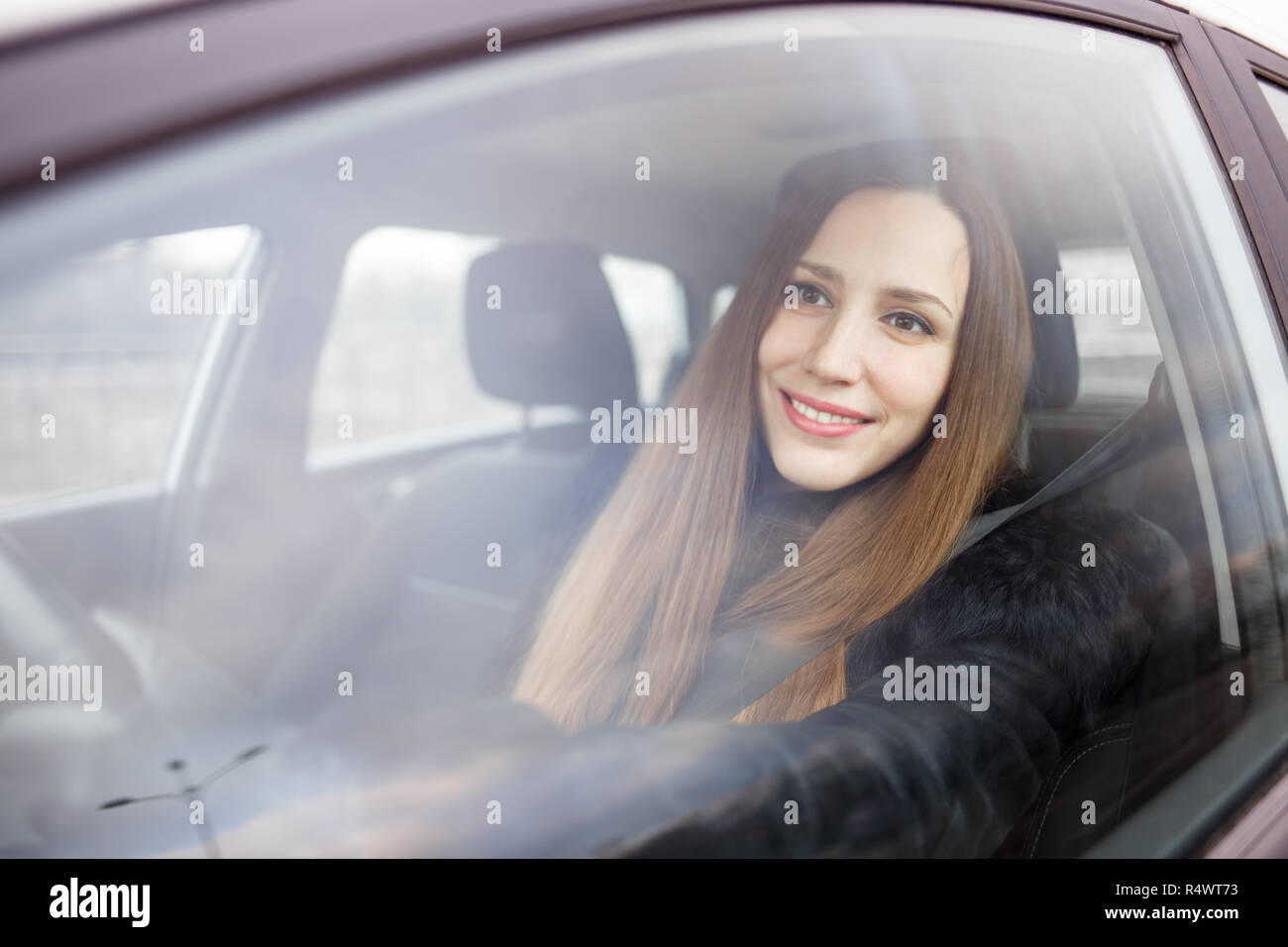 Young lady driving a car in winter. Smiling woman steering car view ...