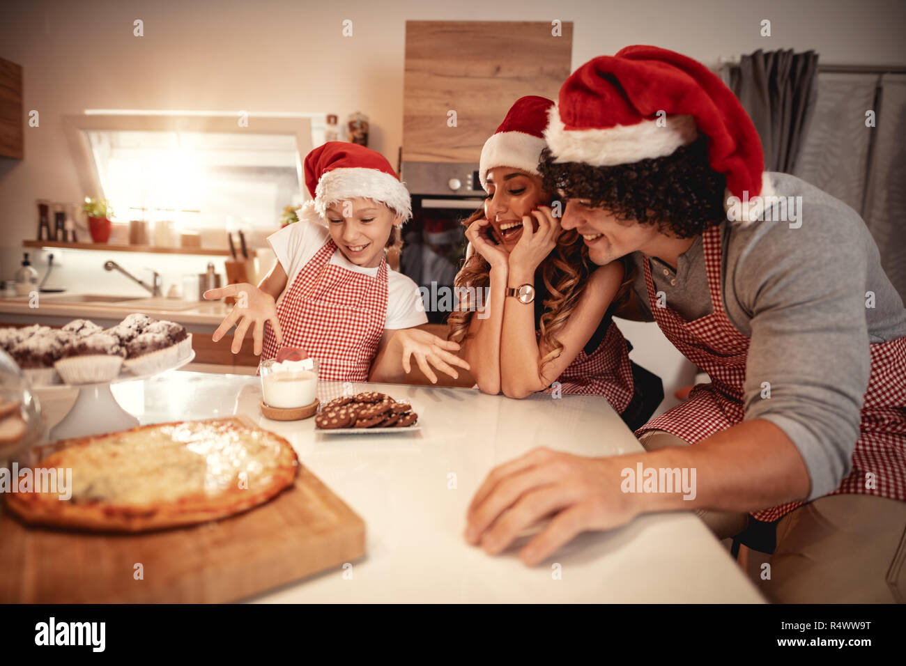 Happy parents and their daughter with santa's cap are preparing meal ...