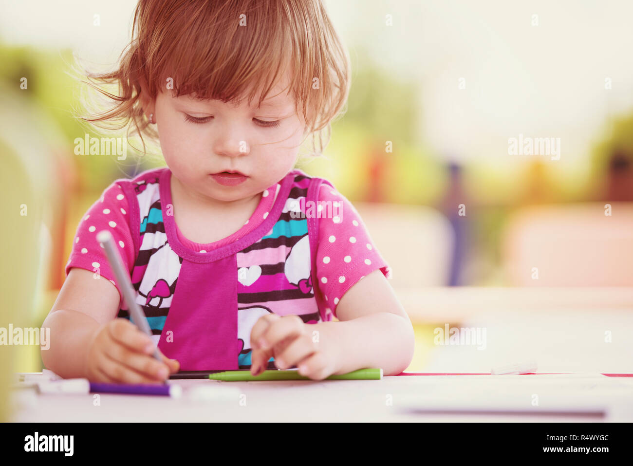 cute little girl cheerfully spending time using pencil crayons while ...