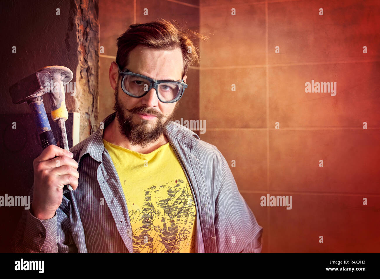 Bearded master in protective glasses holds a sledgehammer and a chisel ...