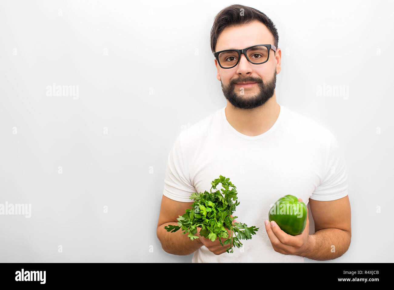 Berded guy in glasses stands and holds green papper and parsley in ...