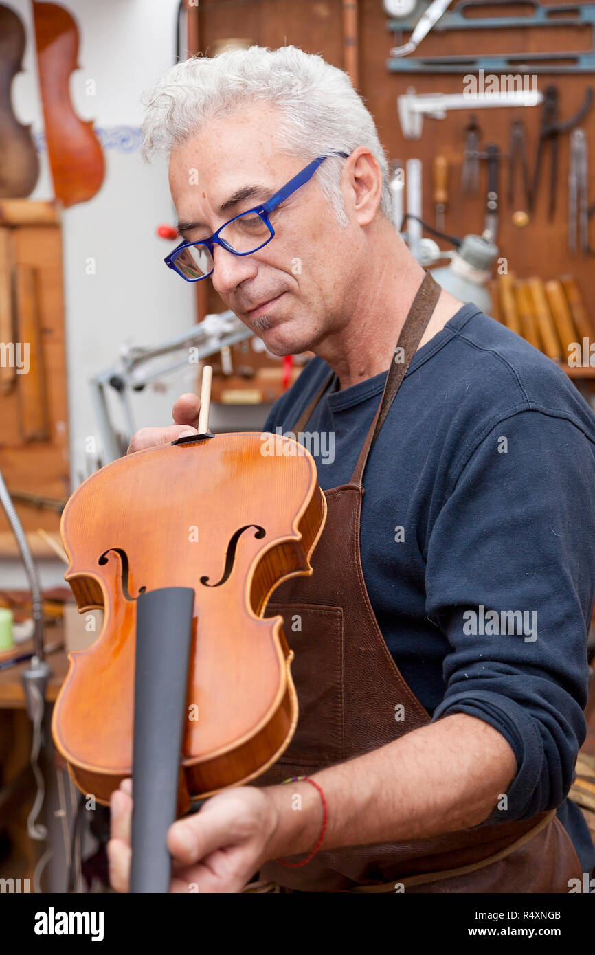 portrait of mature violin maker while testing the violins in his ...