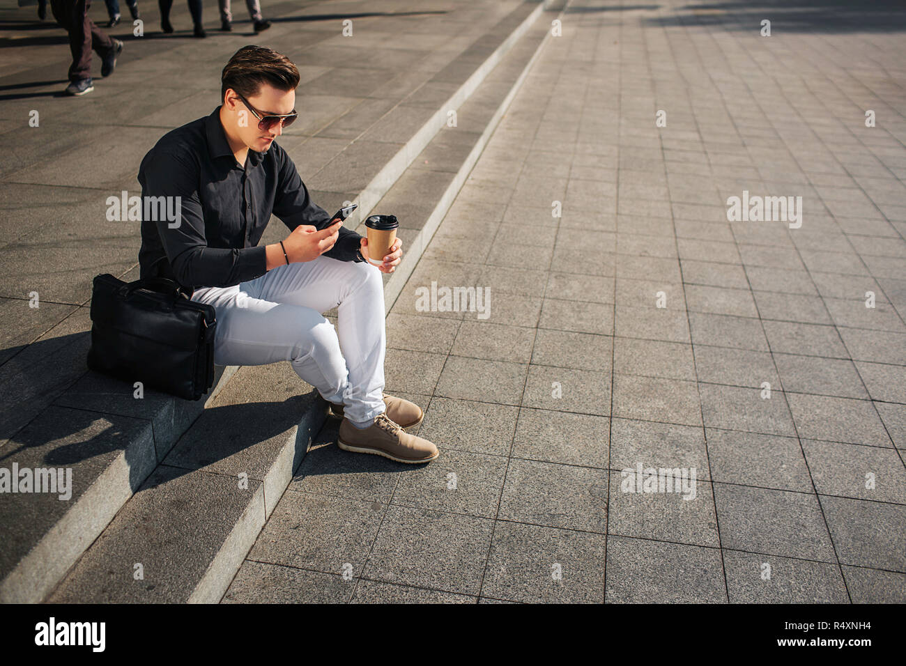 Well-dressed young man sit on steps outside and look at phone. He hold ...