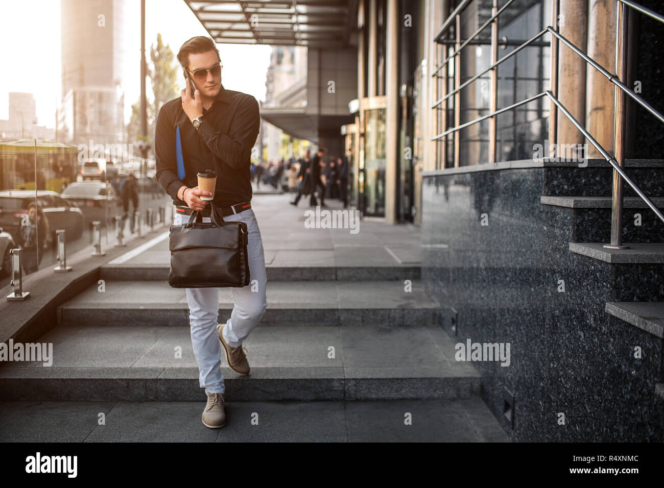 Young businessman walks on steps. He holds phone close to ear and care ...