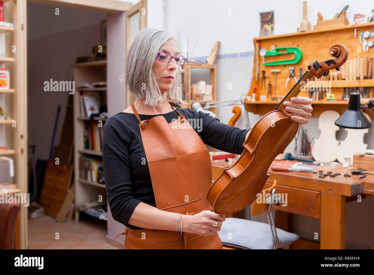 portrait of female mature violin maker while testing the violins in his ...